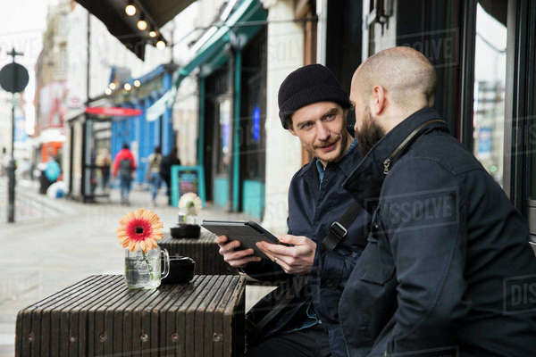 Two men sitting at outdoor cafe table looking at tablet - Royalty-free ...