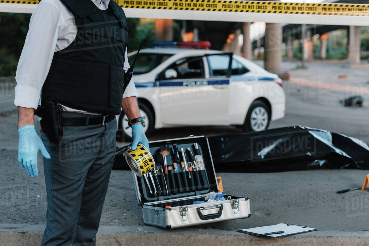 partial view of policeman in latex gloves holding police line at crime ...