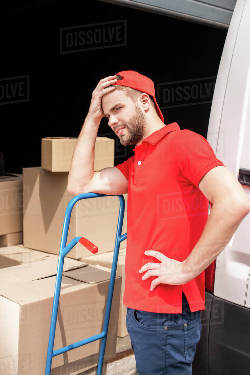 young delivery man in red uniform leaning on delivery cart - Royalty ...