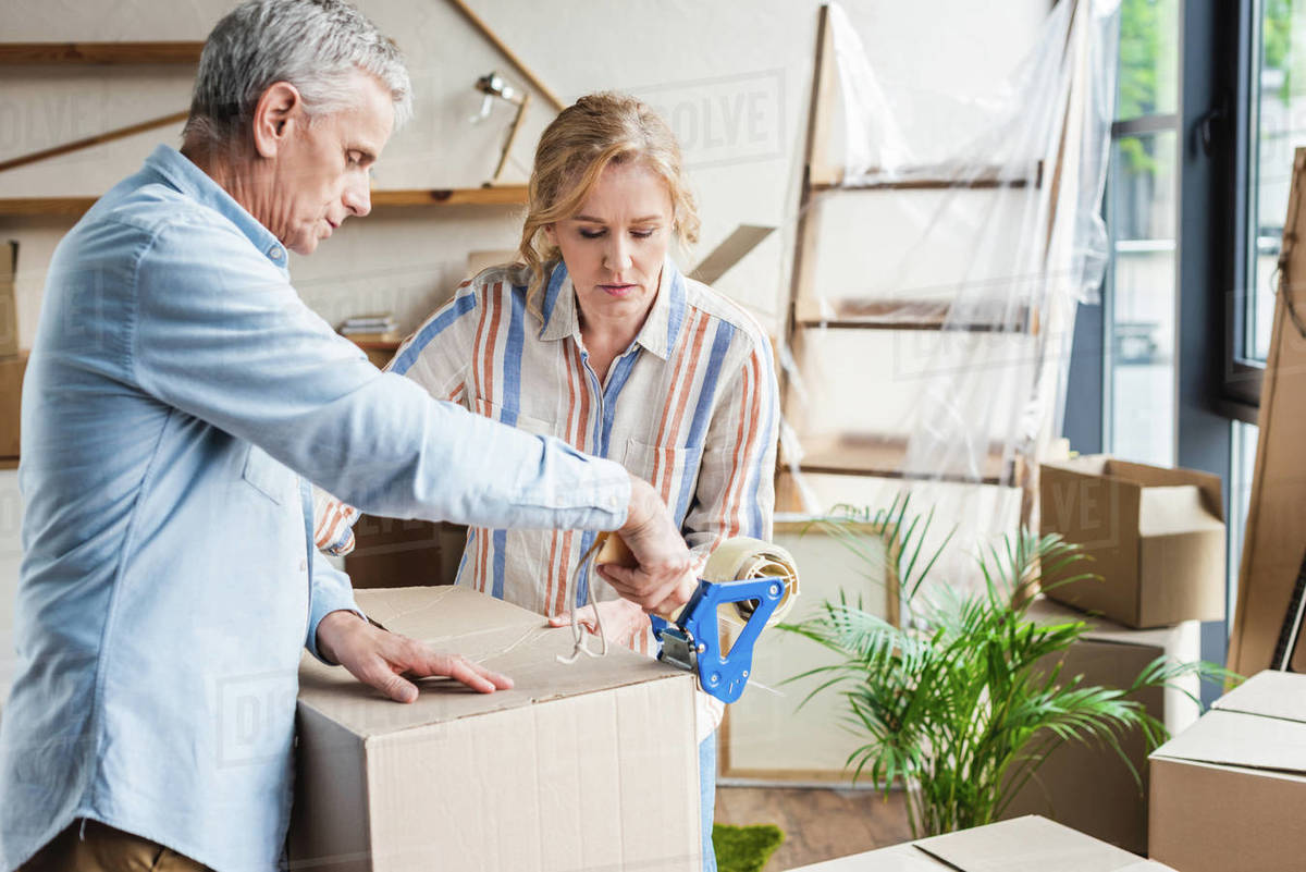 focused senior couple packing cardboard boxes while moving home ...