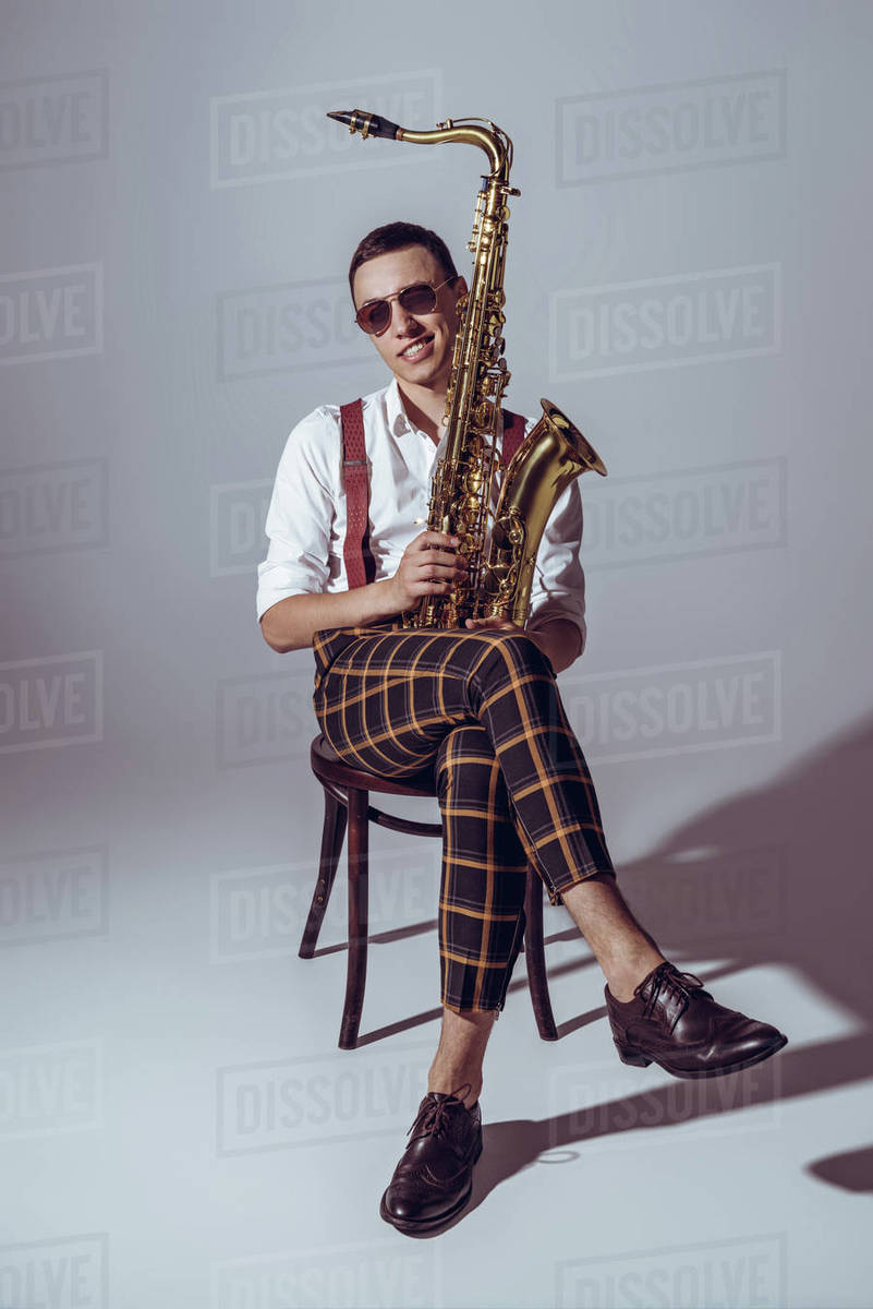 Handsome young saxophonist in sunglasses smiling at camera while ...