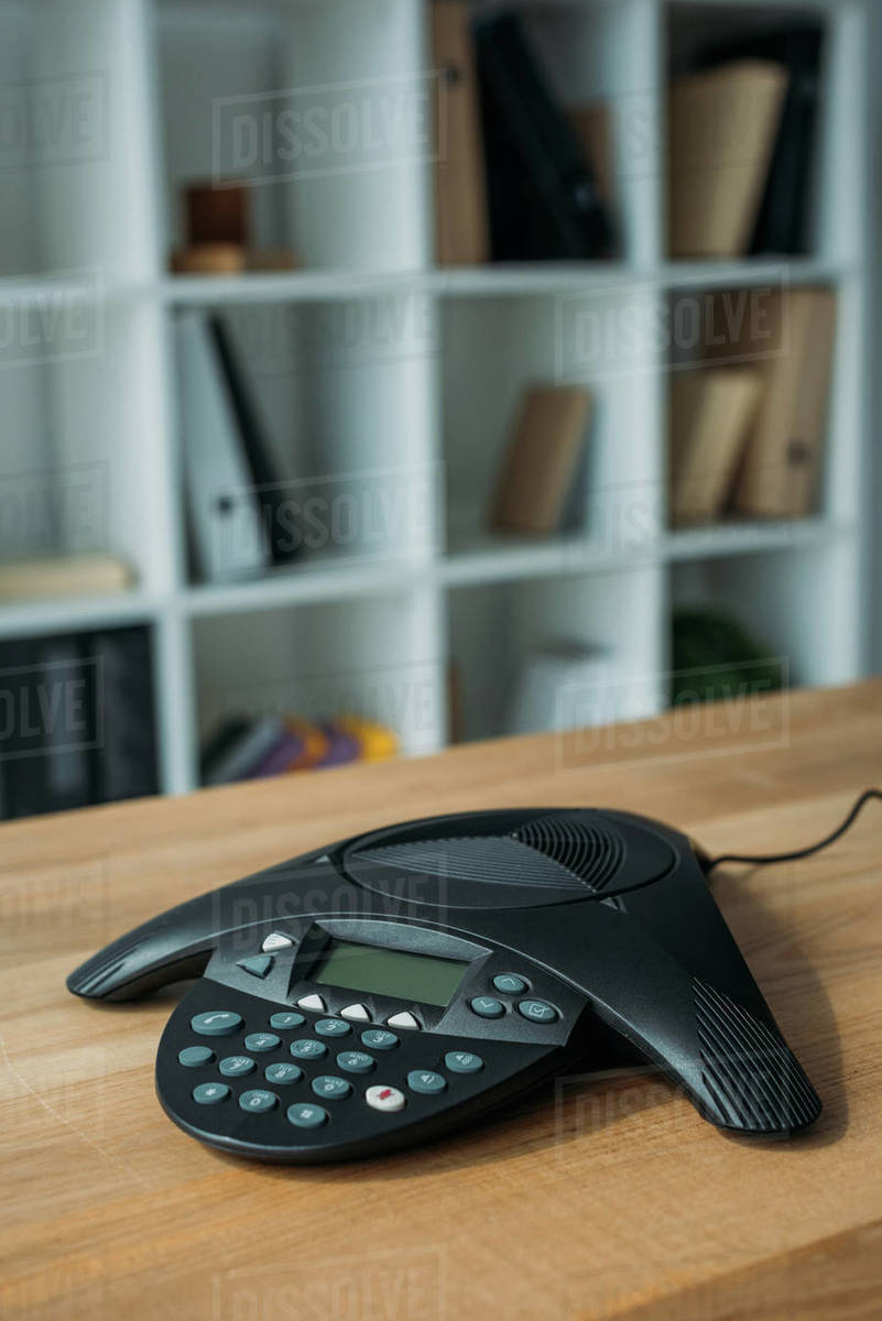 Speakerphone on wooden table at office with blurred bookshelves on ...