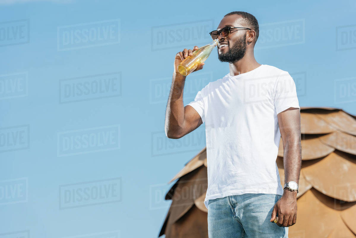 smiling handsome african american man drinking soda against blue sky ...