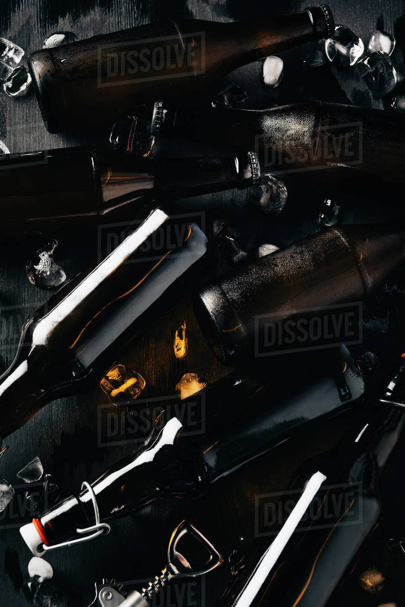 flat lay with bottle opener, glass bottles of beer and ice cubes ...