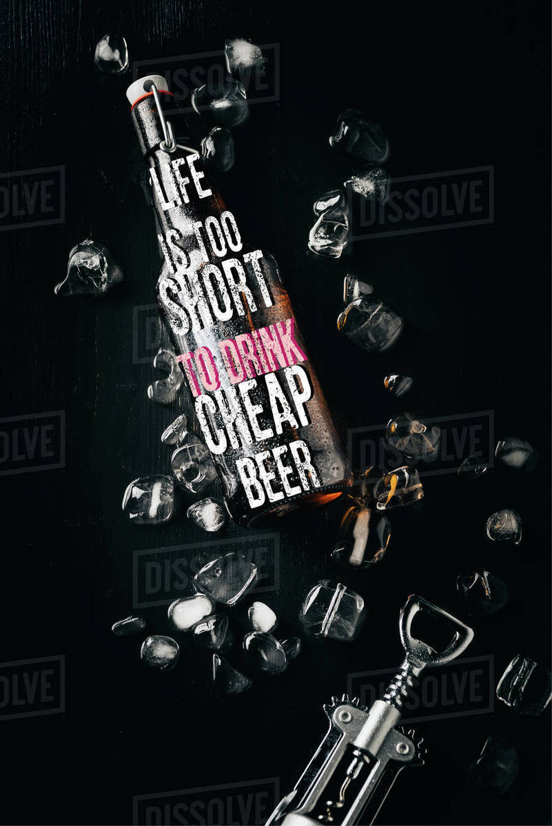 flat lay with bottle opener, bottle of beer on ice cubes arranged on ...