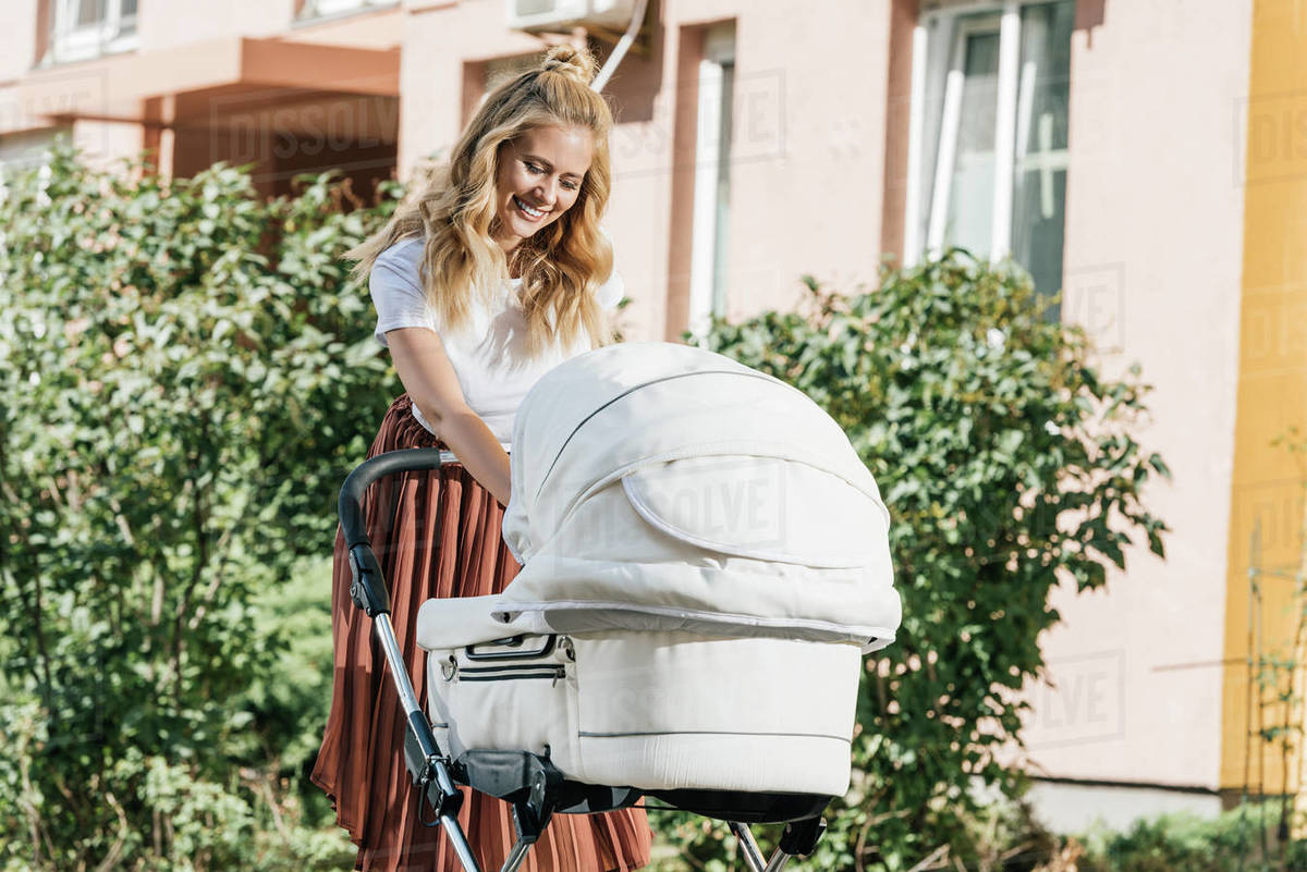 Attractive happy mother looking at baby stroller on street - Royalty ...