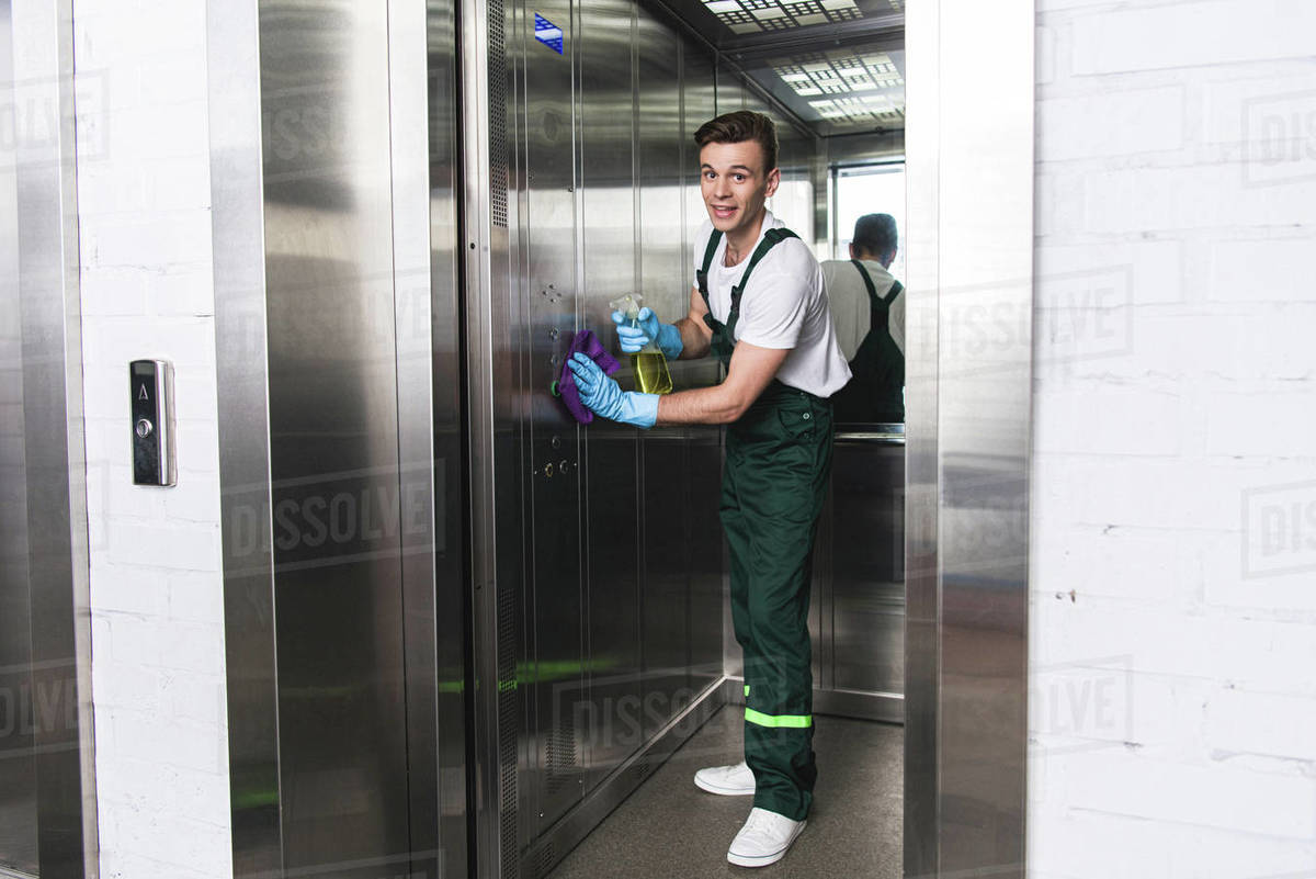 Handsome young man cleaning elevator and smiling at camera - Royalty ...