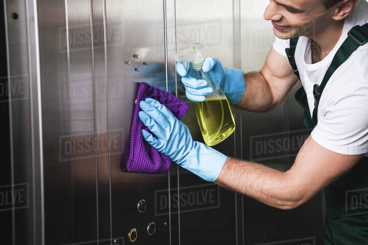 Cropped shot of smiling young worker cleaning elevator with rag and ...