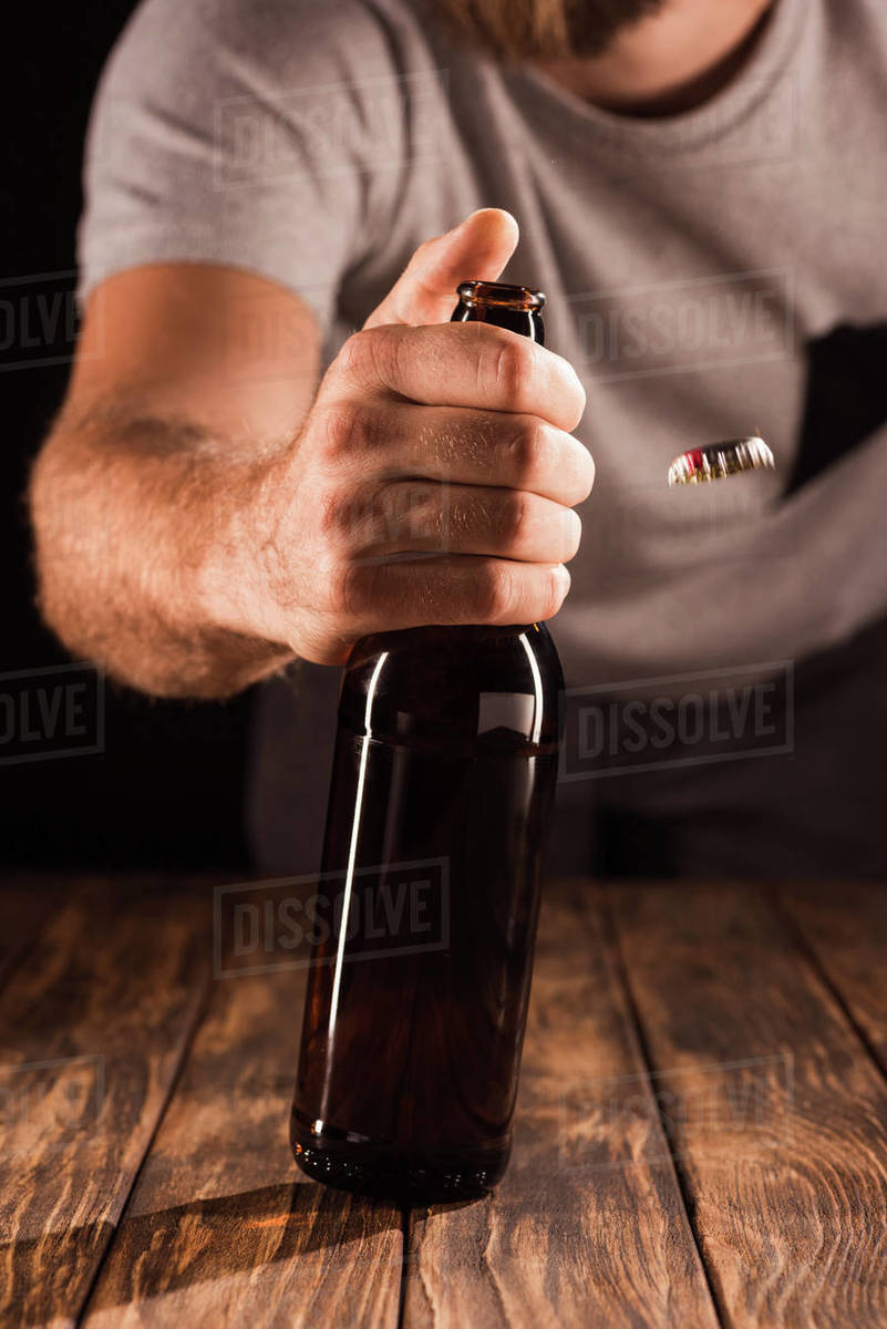 Partial view of man opening beer bottle at wooden table - Royalty-free ...