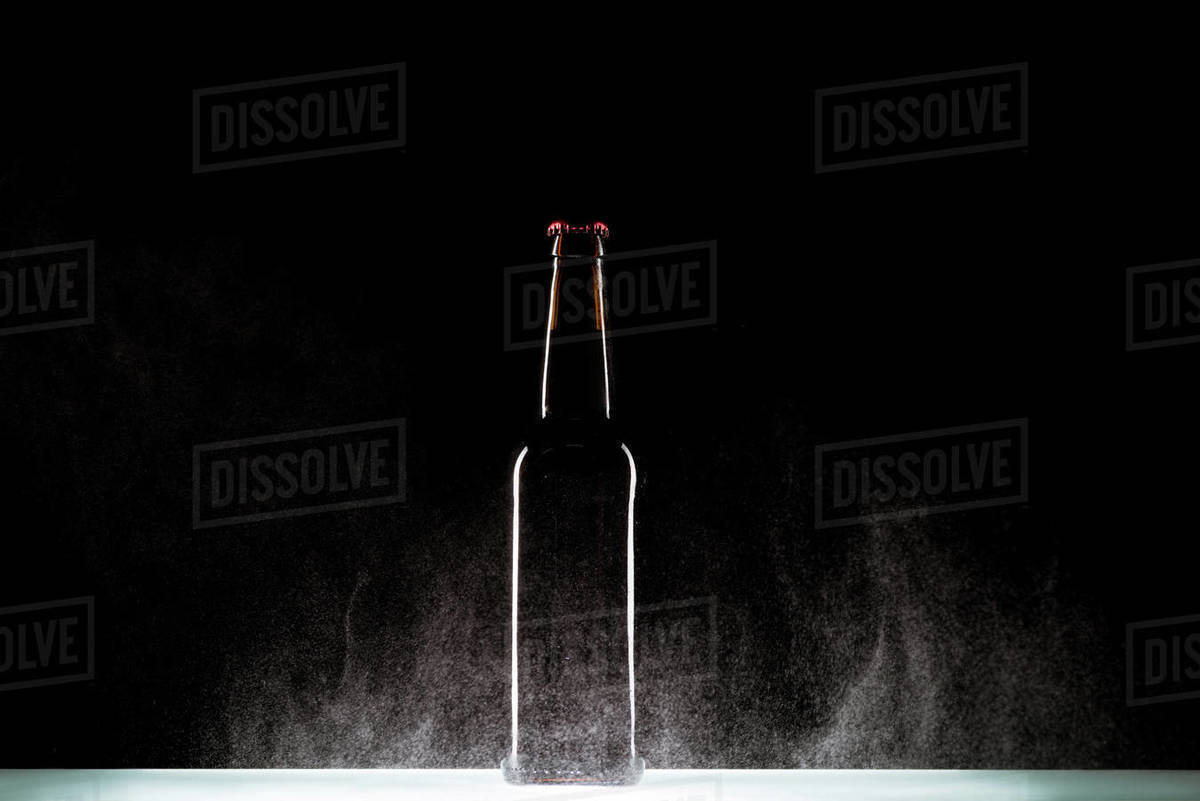Beer bottle with spraying water around at surface on black background ...
