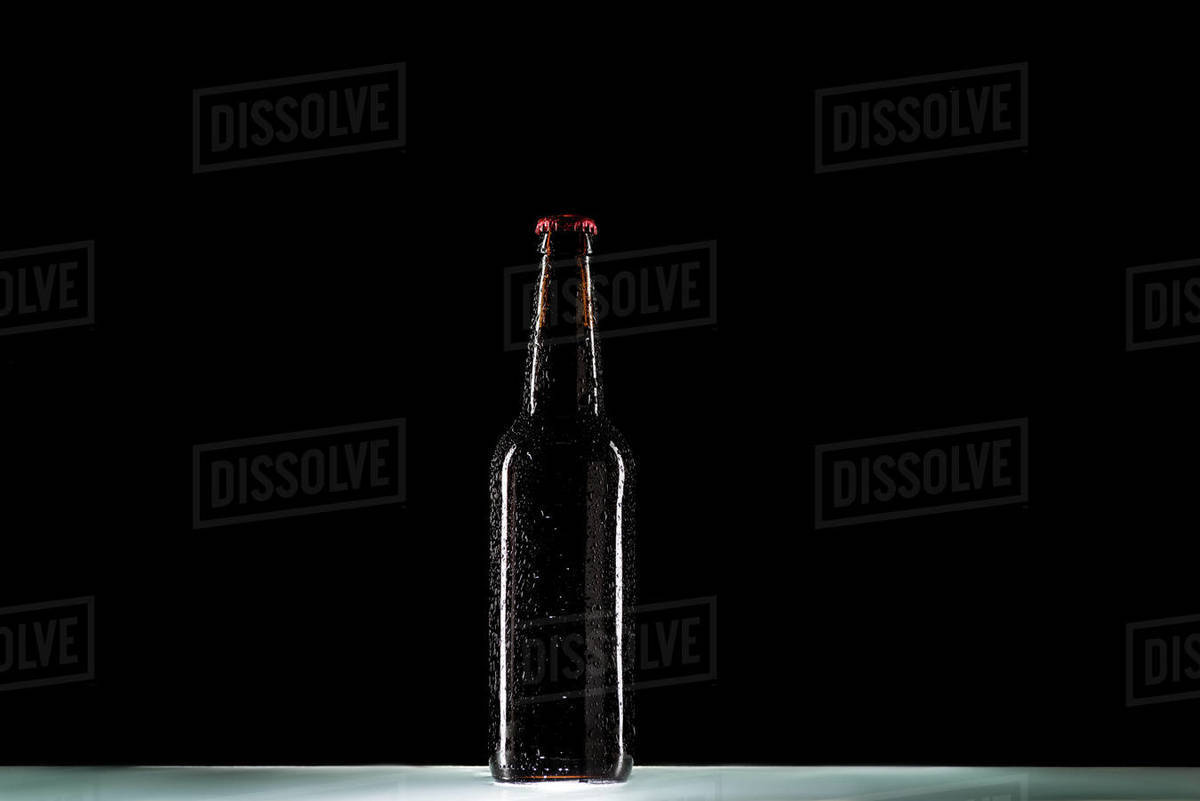 Close up view of beer bottle at tabletop on black background ...
