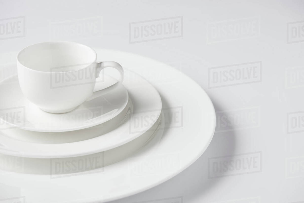 Close up image of cup on stack of different plates on white table ...