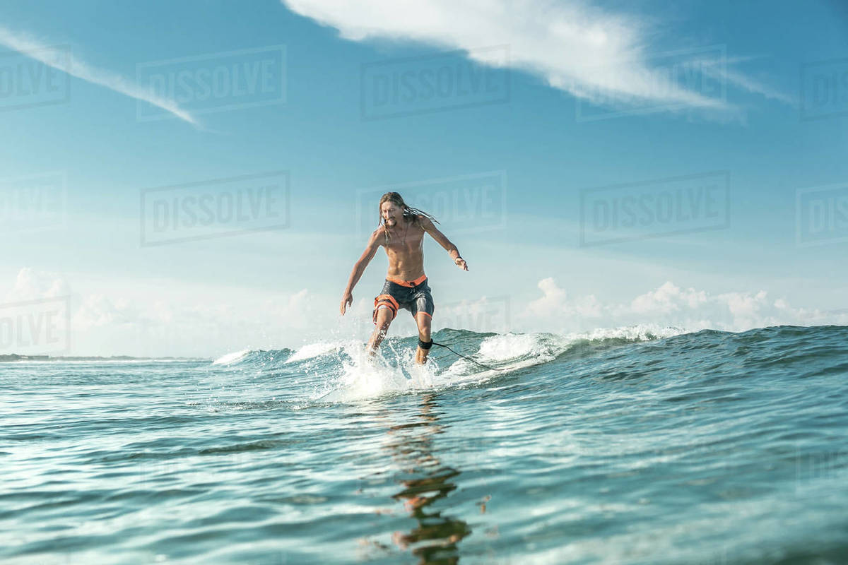 Shirtless male surfer riding on surfing board in ocean at Nusa Dua ...