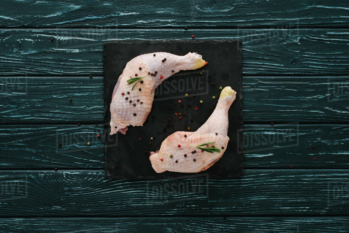 top view of chicken legs with pepper corns on black slate - Royalty ...