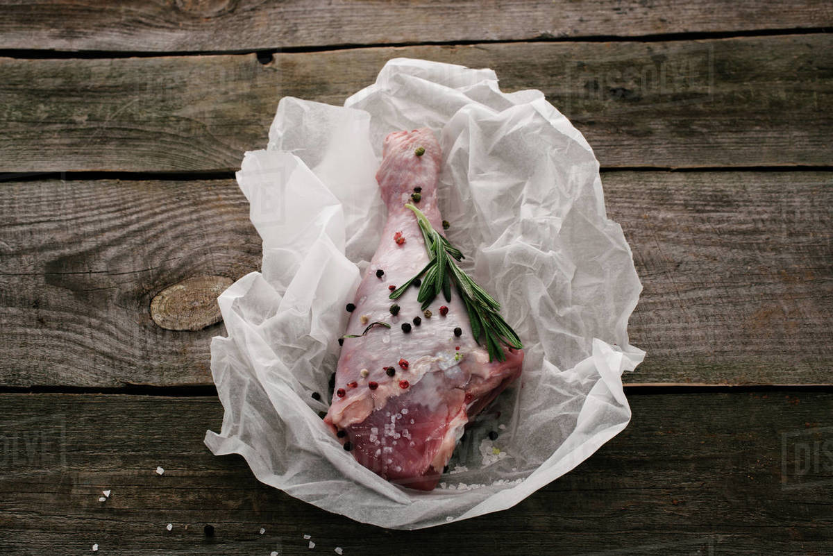 uncooked turkey leg with pepper corns and rosemary on baking paper on ...