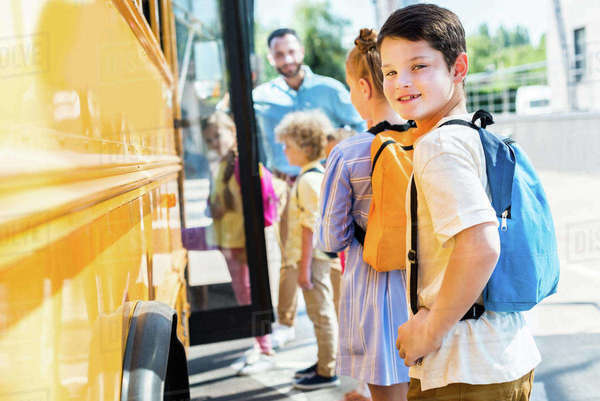 little schoolboy entering school bus with classmates while teacher ...