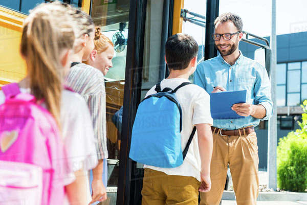pupils entering school bus while teacher writing in clipboard - Royalty ...
