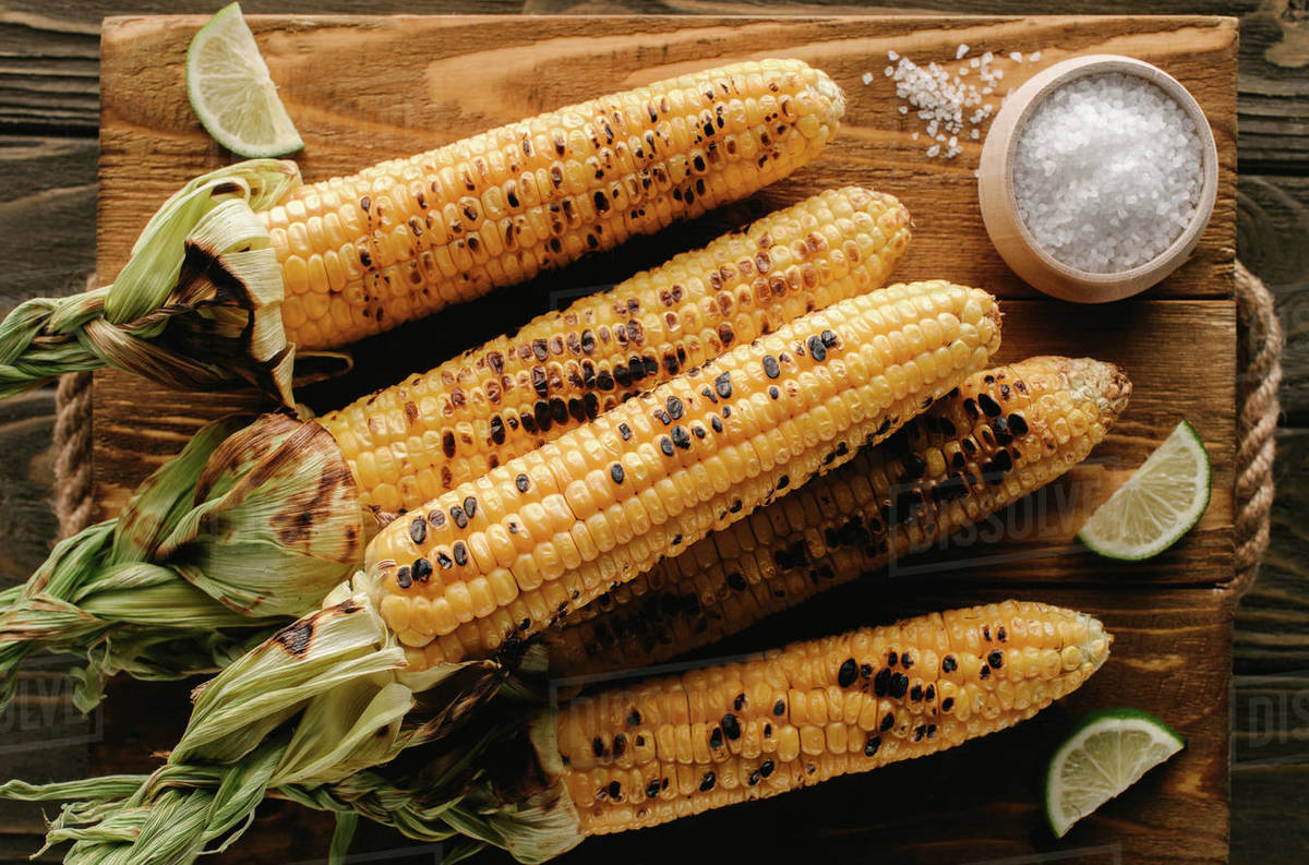 Top view of cutting board with grilled corn, lime slices and salt on ...
