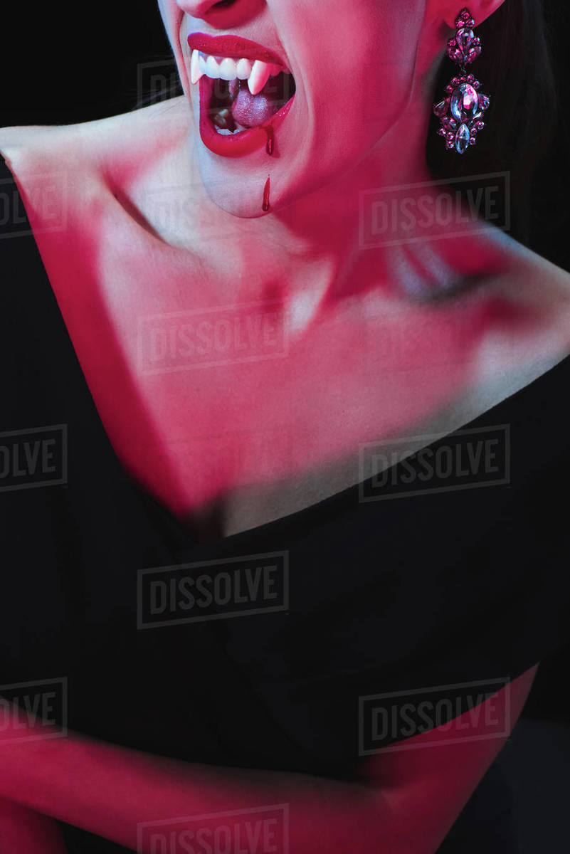 Cropped view of vampire woman showing her vampire fangs on dark ...