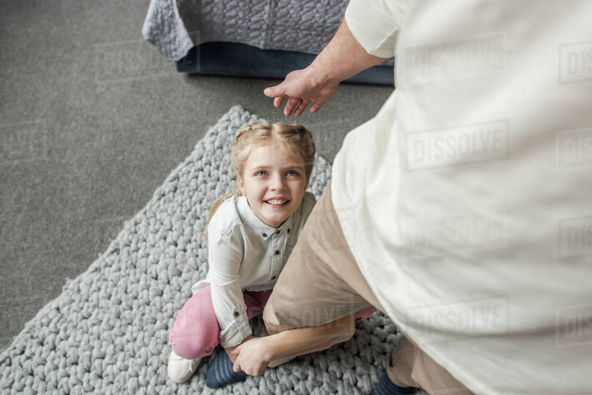 Happy adorable daughter sitting on floor and hugging father's leg ...