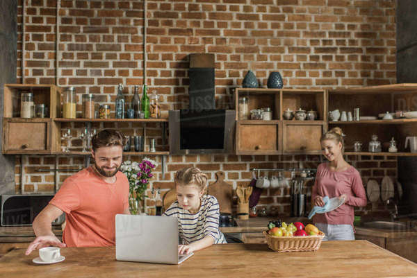 Cute little girl using laptop with parents in kitchen - Royalty-free ...