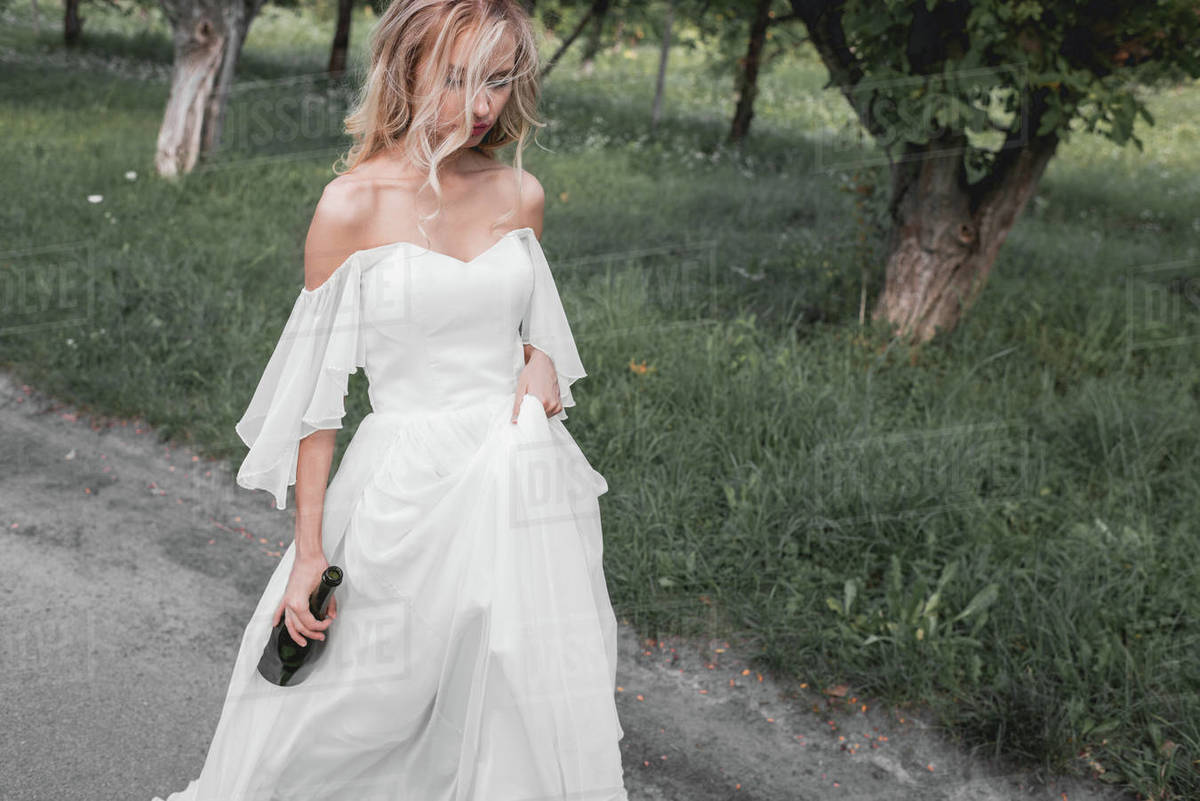 high angle view of upset young bride in wedding dress holding bottle of ...