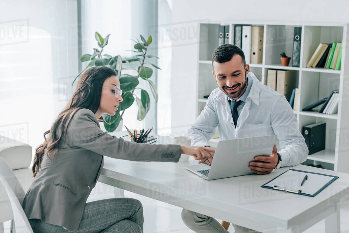 side view of patient pointing on laptop to doctor in clinic - Royalty ...