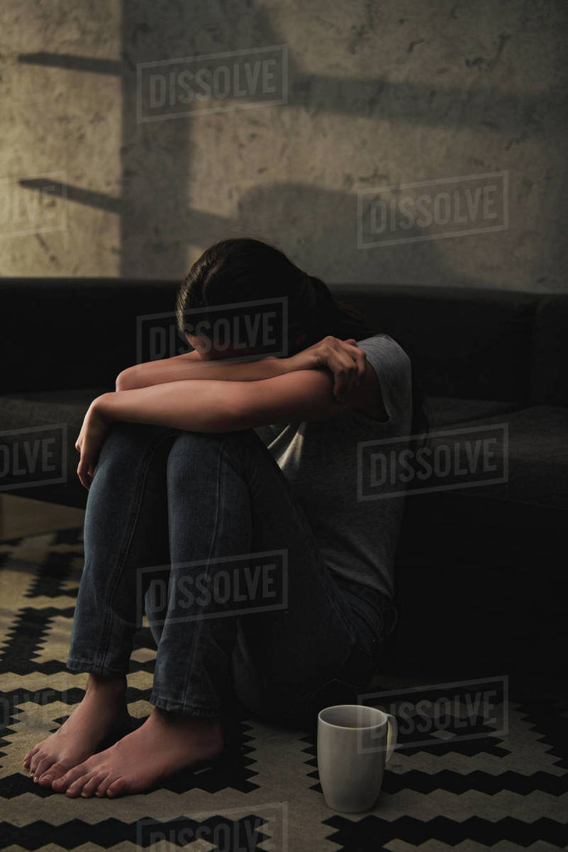 emotional crying woman hugging her knees while sitting on floor at sofa ...