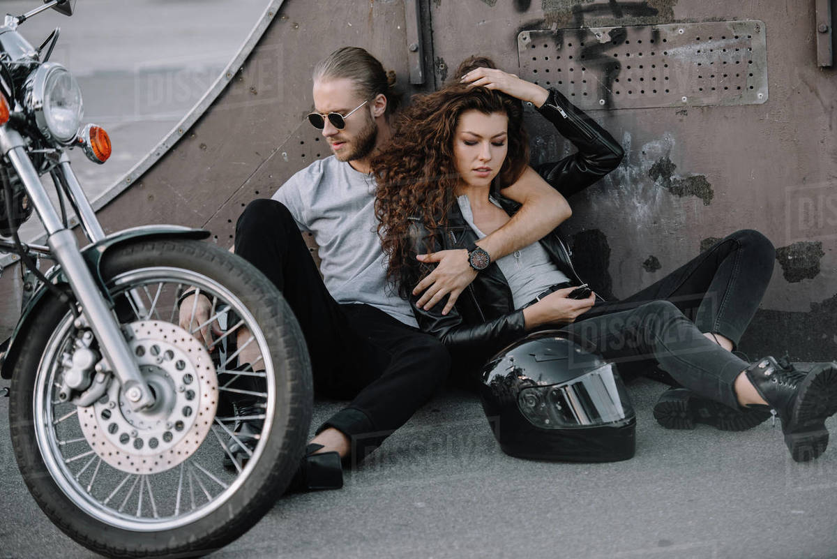 Couple of bikers hugging and sitting on asphalt with helmet and ...