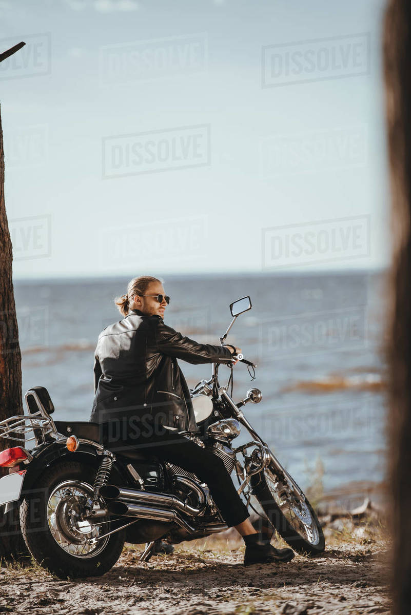Biker in black leather jacket sitting on chopper motorcycle near the ...