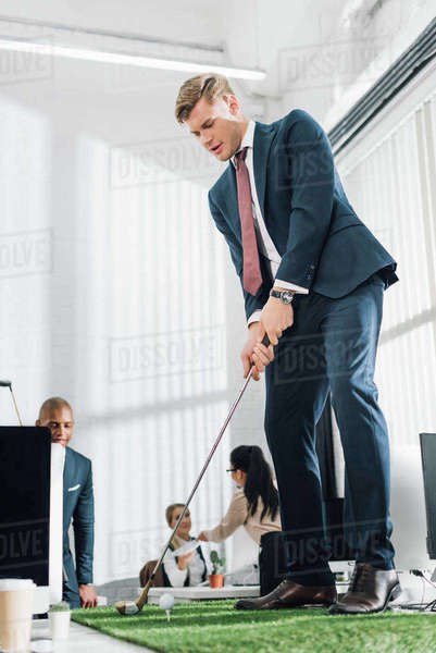 Low angle view of young businessman playing golf in office - Royalty ...