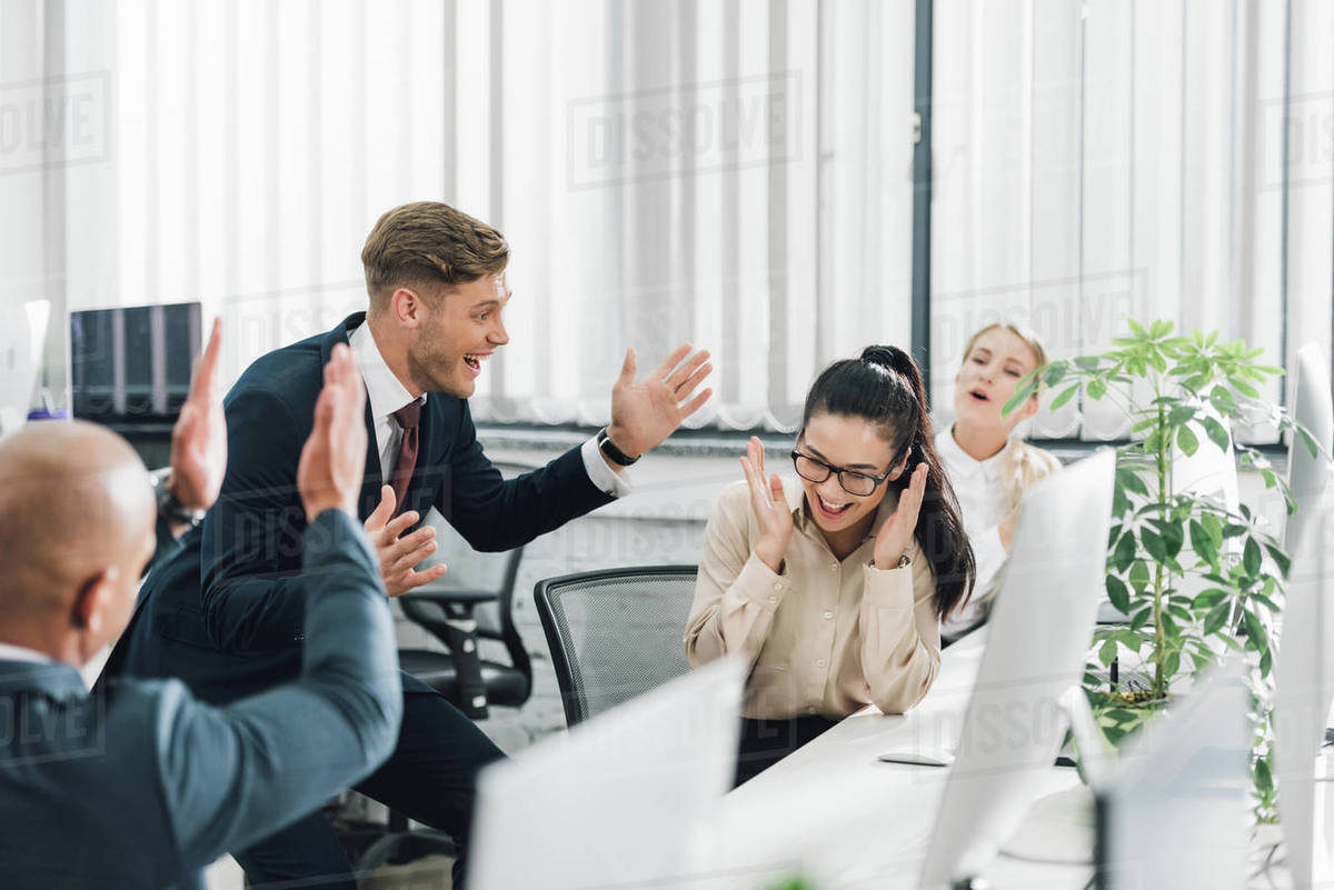 Excited young business colleagues celebrating good news in office ...