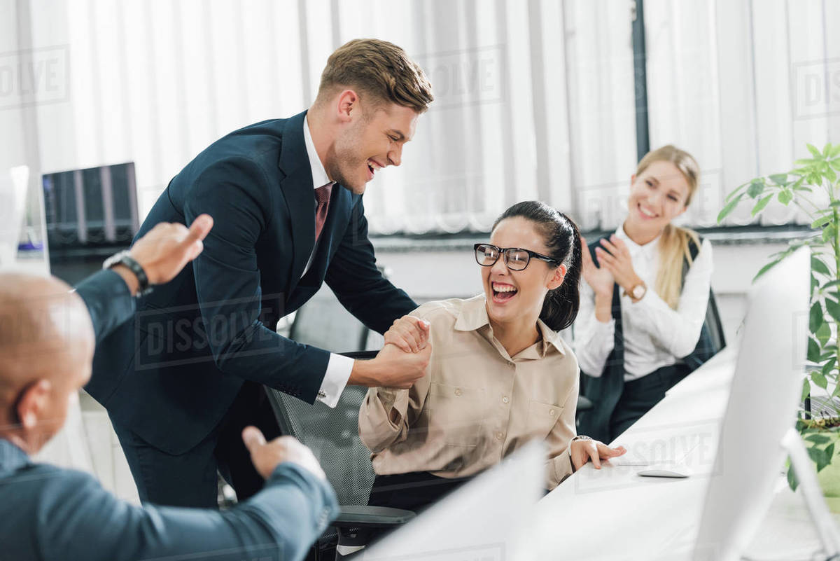 Cheerful young business people greeting happy colleague in office ...