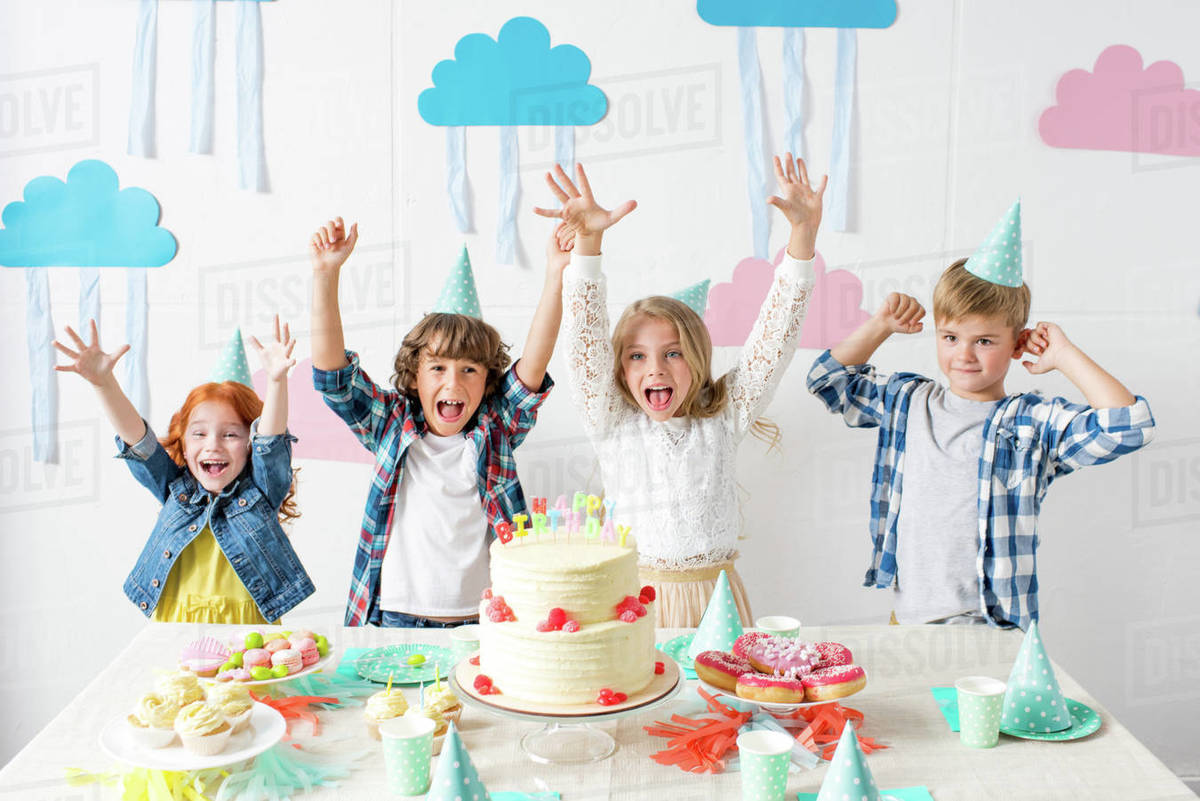 adorable happy kids raising hands and smiling at camera at birthday ...