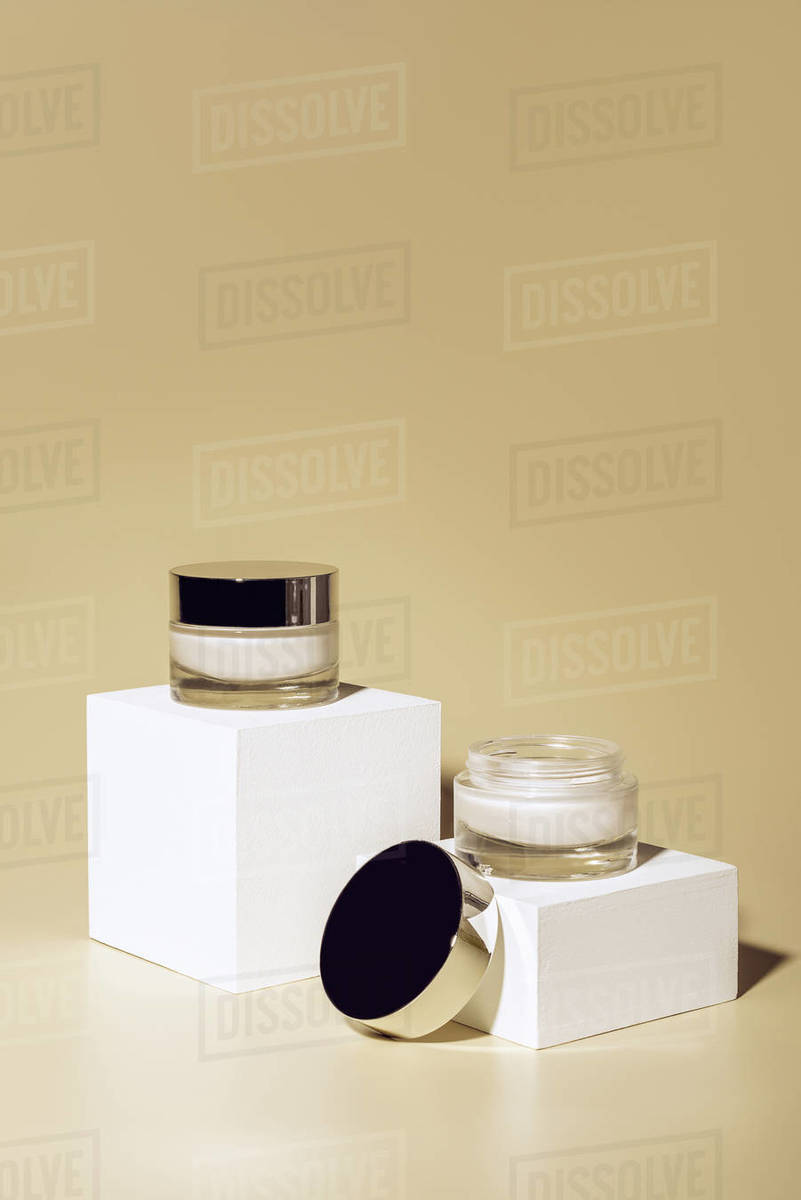 close up view of facial and body creams in glass jars on white cubes on ...