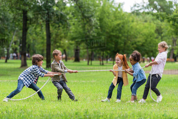 side view of cute little multiethnic children pulling rope in park ...