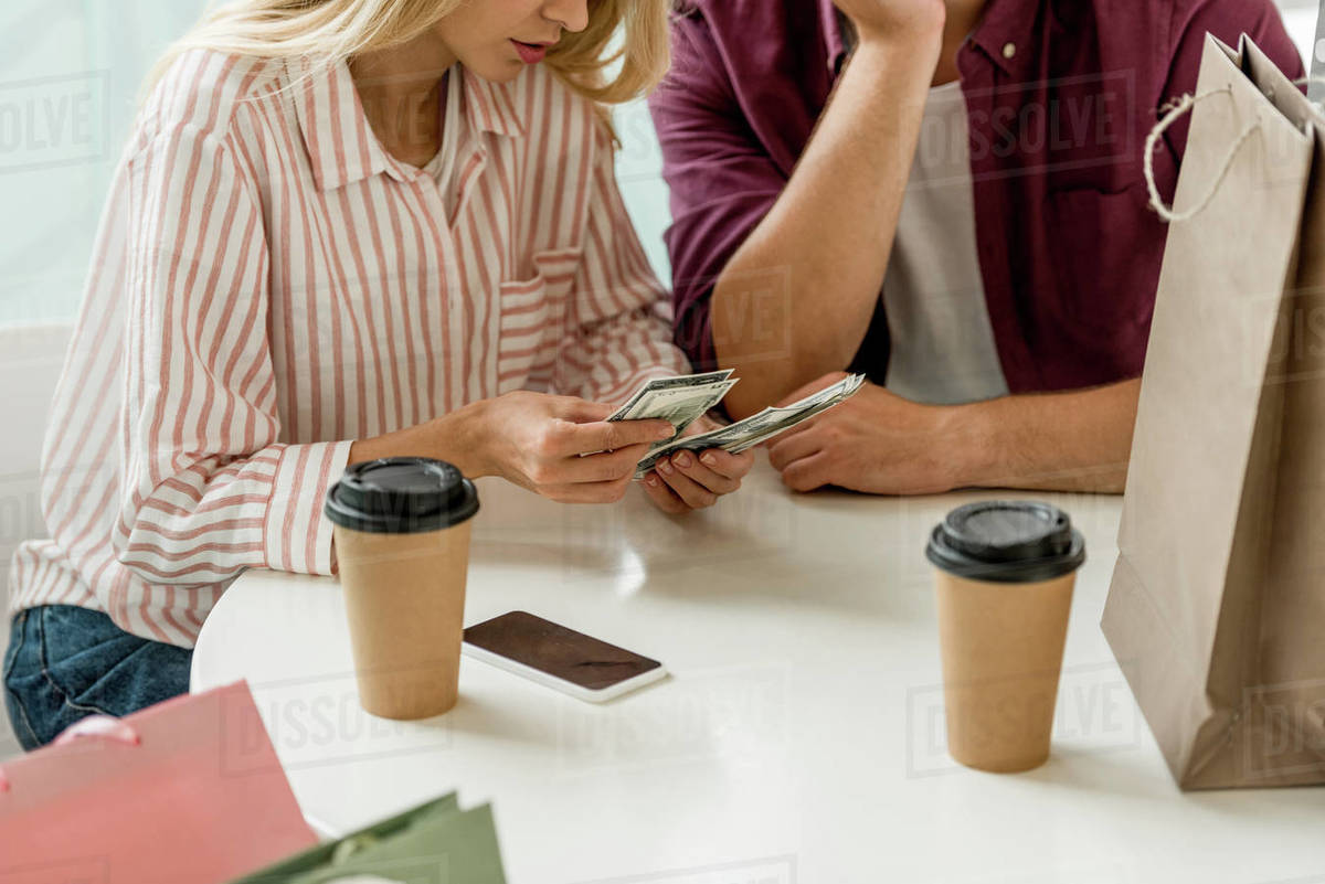 partial view of young couple counting cash money at table with coffee ...