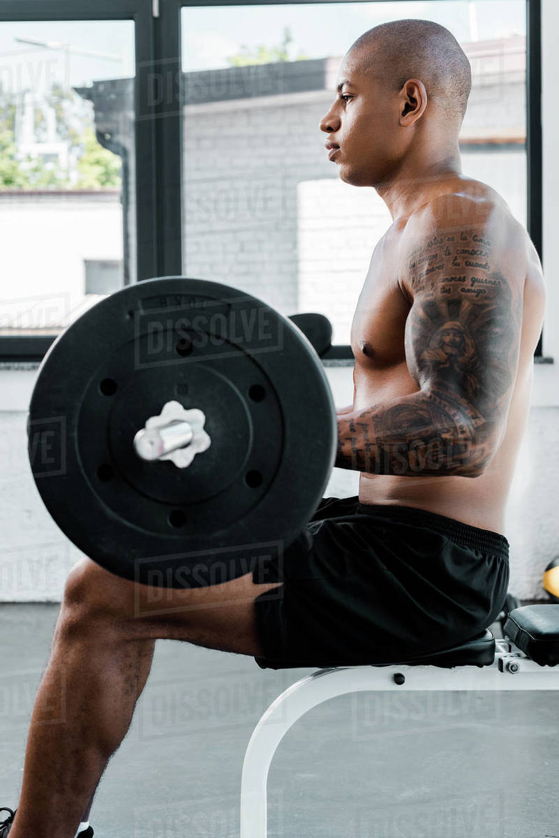 side view of muscular tattooed sportsman sitting on bench and holding ...