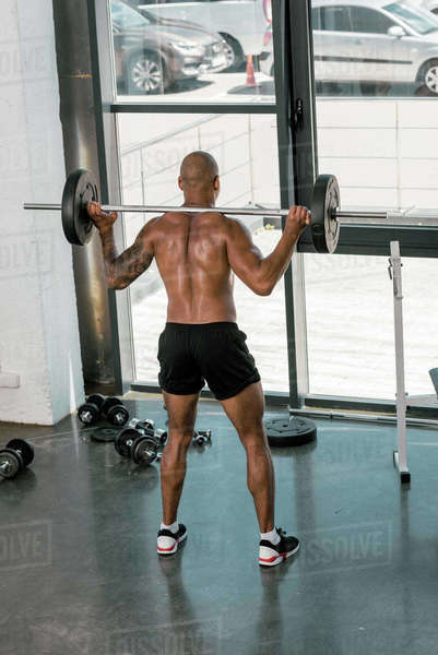 back view of athletic young shirtless man lifting barbell in gym ...