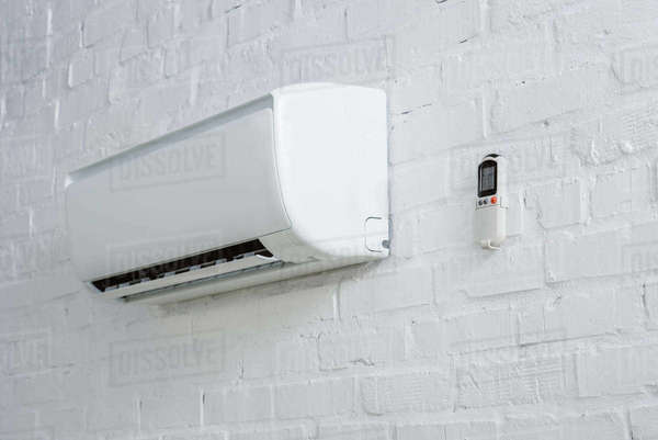air conditioner hanging on white brick wall with remote control ...