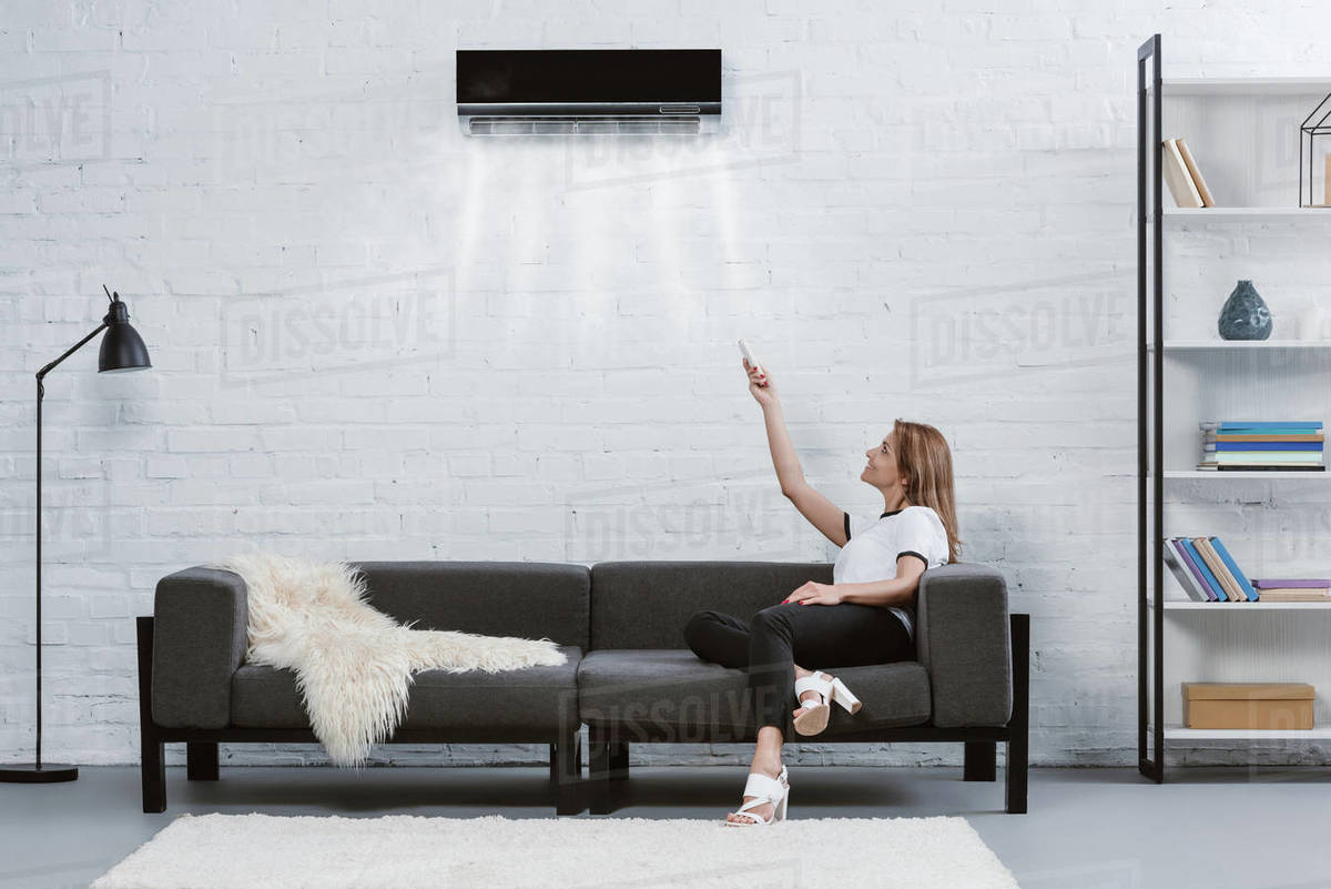 happy young woman pointing at air conditioner hanging on wall with ...