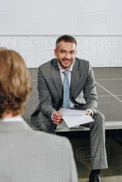 smiling handsome business coach sitting on stage during training in hub ...