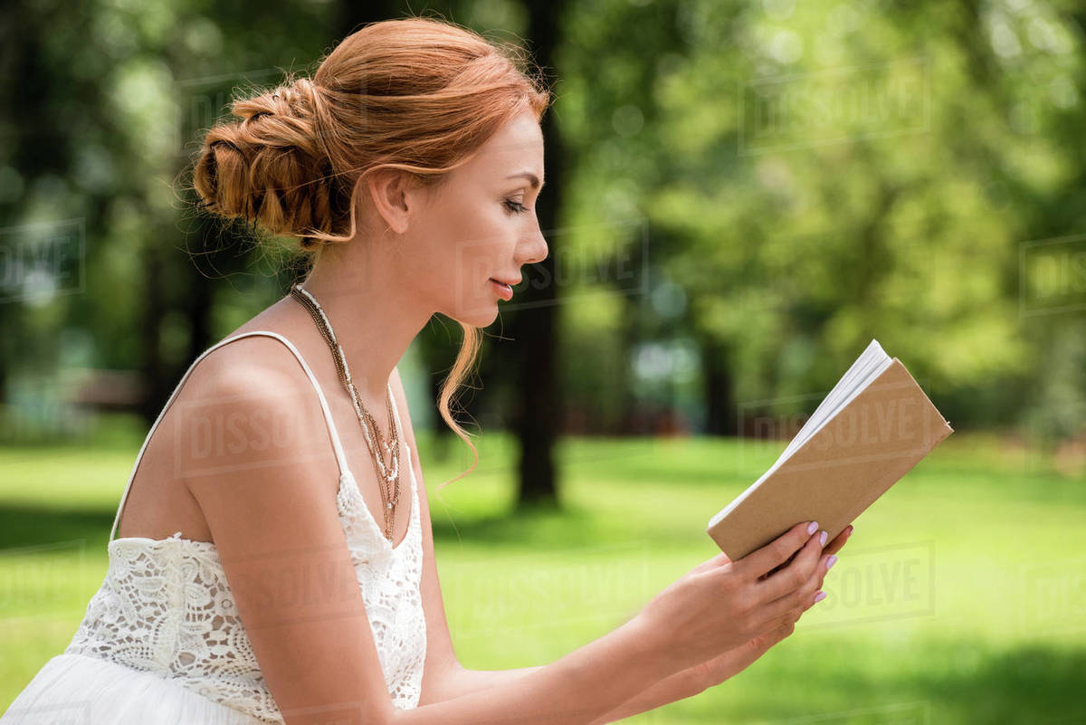 Profile Portrait Of Beautiful Young Blonde Woman Reading Book At Park