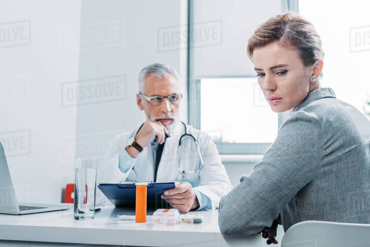 Sad female patient looking away while mature male doctor sitting near ...