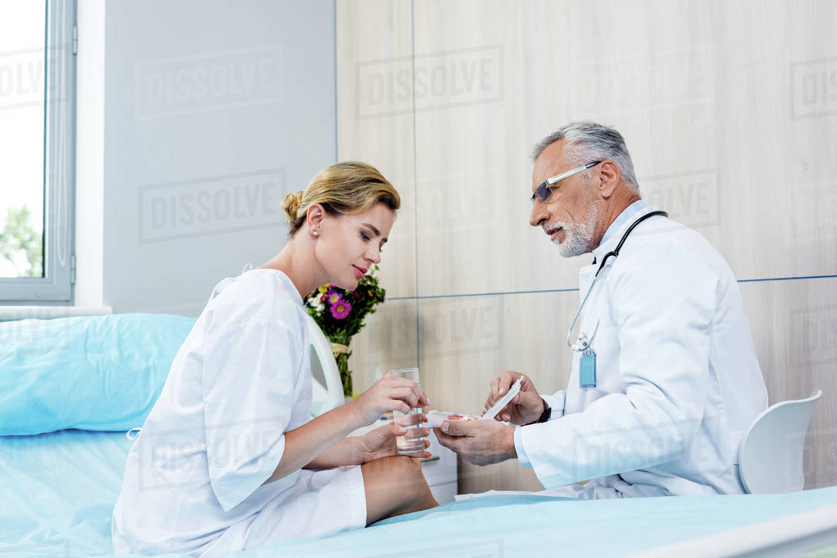 Adult female patient with glass of water taking pills from mature male ...