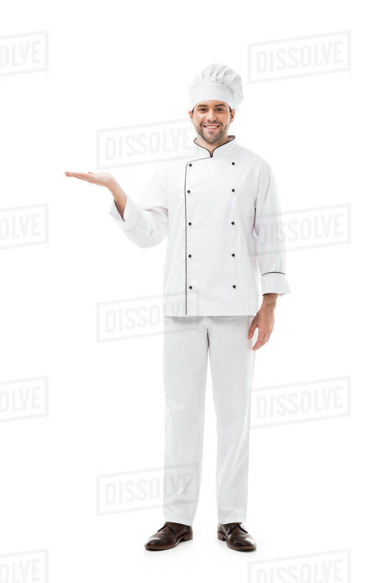 Smiling young chef pointing at blank space and looking at camera ...