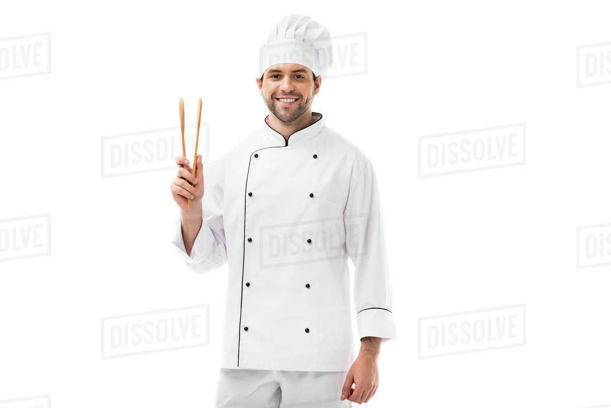 Happy young chef with wooden tongs looking at camera isolated on white ...