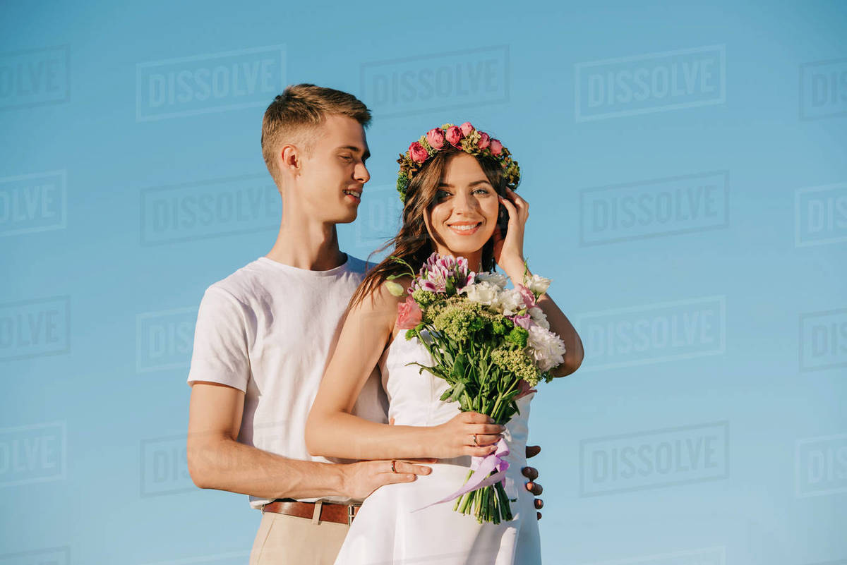 Beautiful wedding couple holding bouquet and posing against blue sky ...