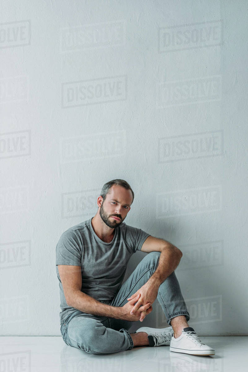 Full length view of sad mid adult man sitting on floor and looking at ...