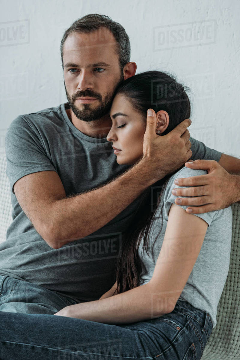 Bearded Man Supporting And Hugging Stressed Sad Woman Sitting On Couch